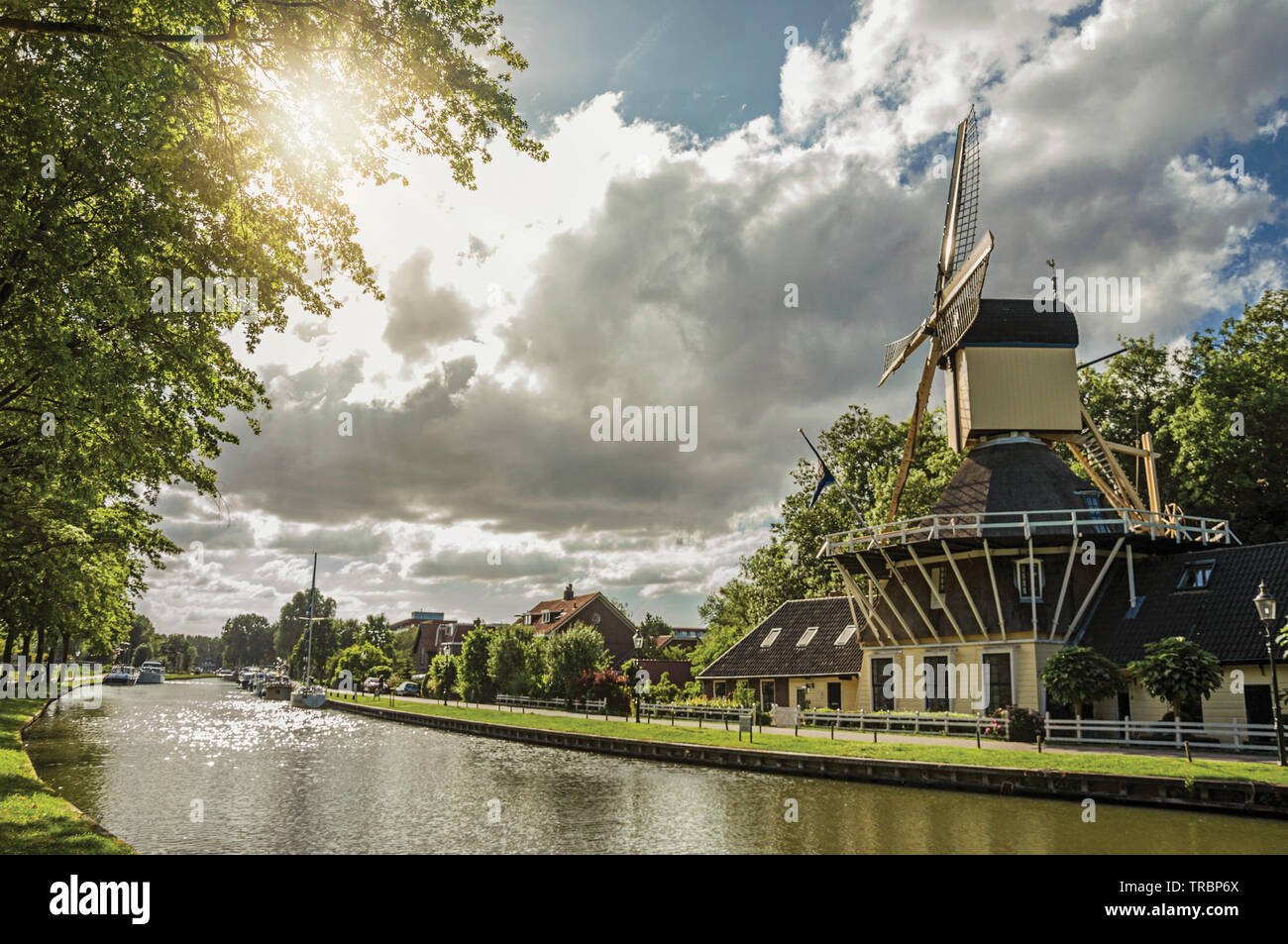 Wide canal with windmill and boats and shine of sunset reflected in ...