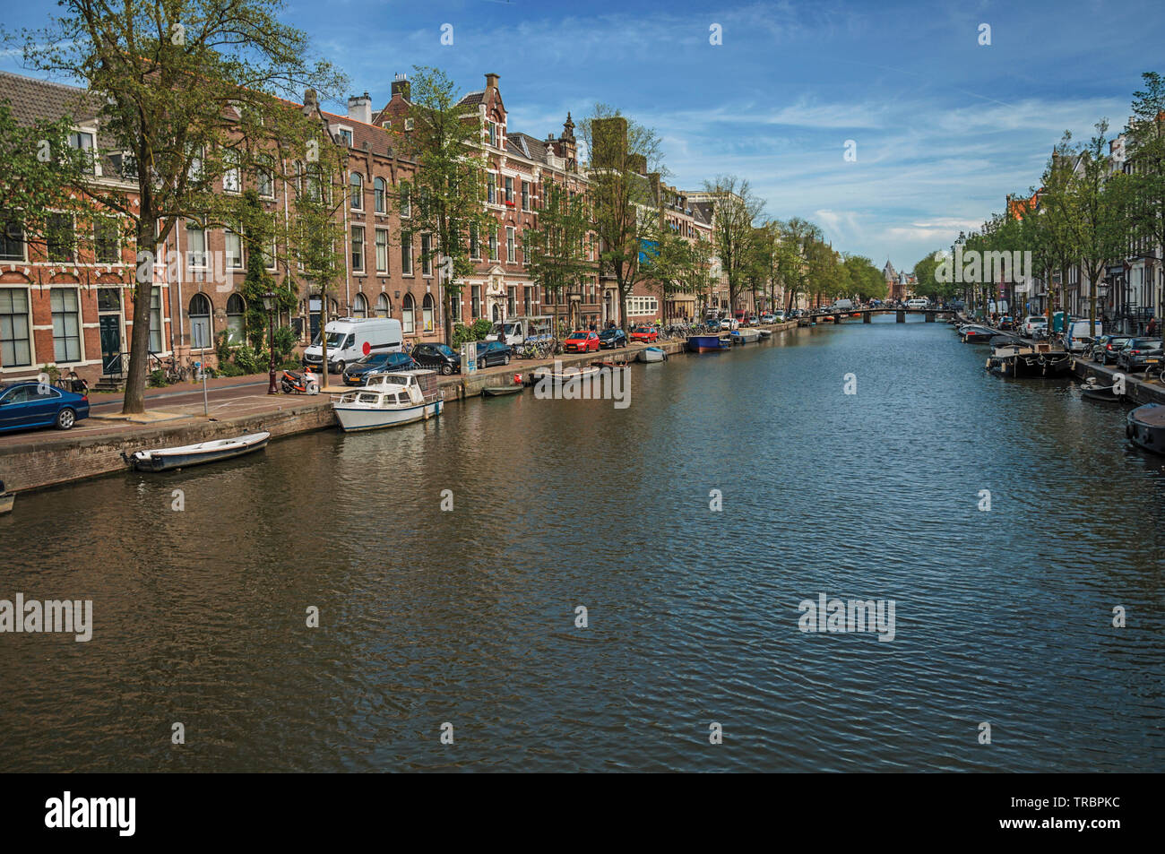 Tree-lined canal with old brick buildings, bridge and moored boats in ...