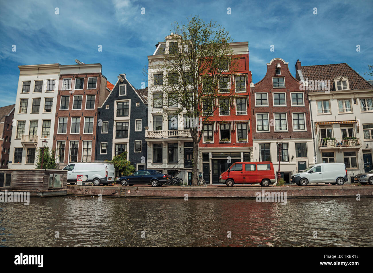 Tree-lined canal with old brick buildings alongside street in Amsterdam ...
