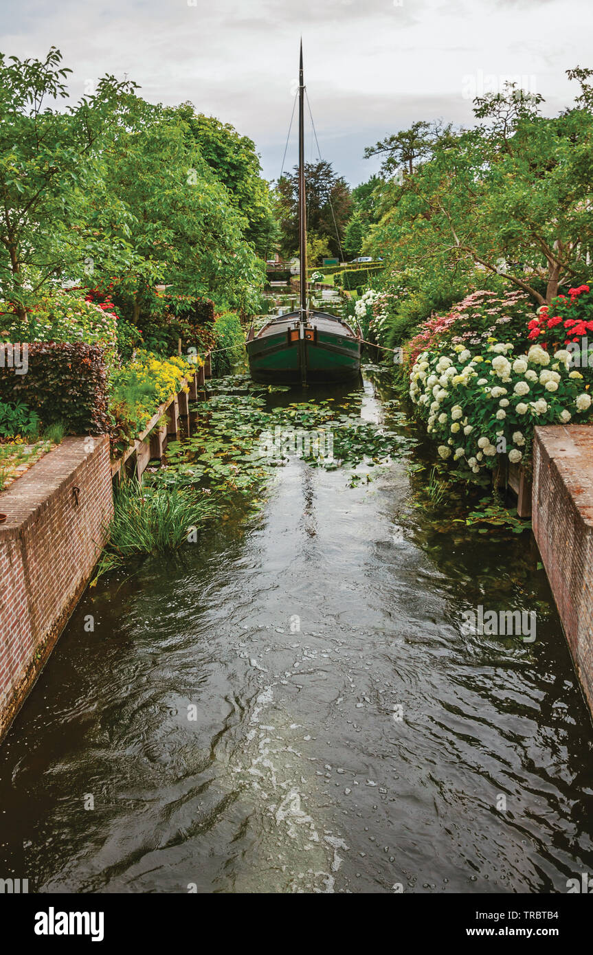 Charming small canal with decorative boat next to lush and flowery ...
