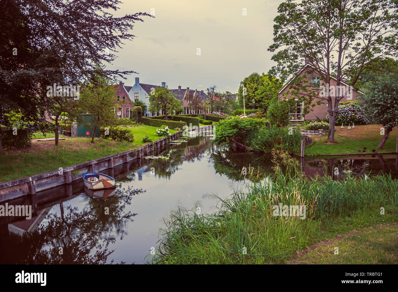 Canal next to rustic houses with gardens and trees reflected on water ...