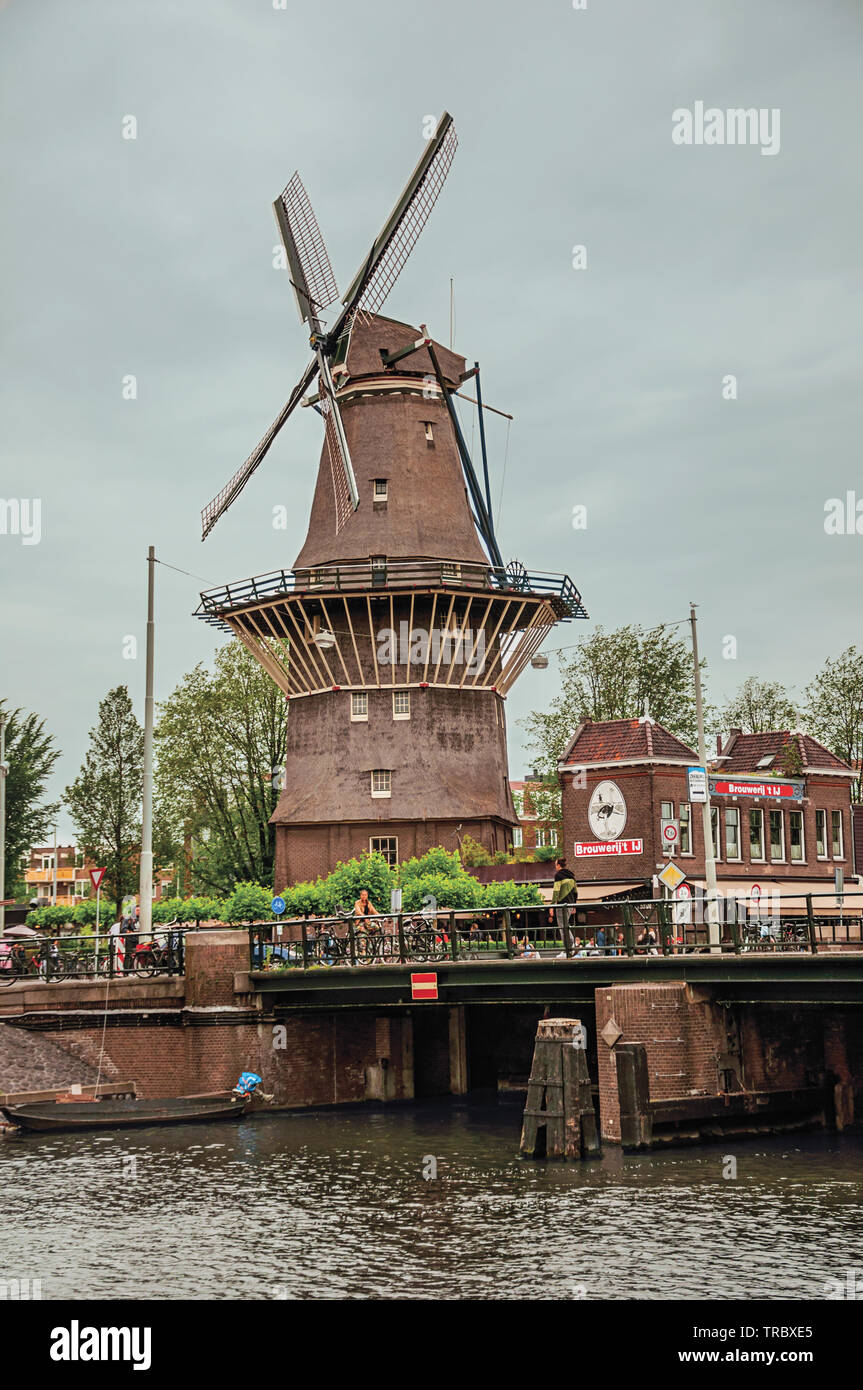 Bridge over canal, trees and old windmill with cloudy sky in Amsterdam ...