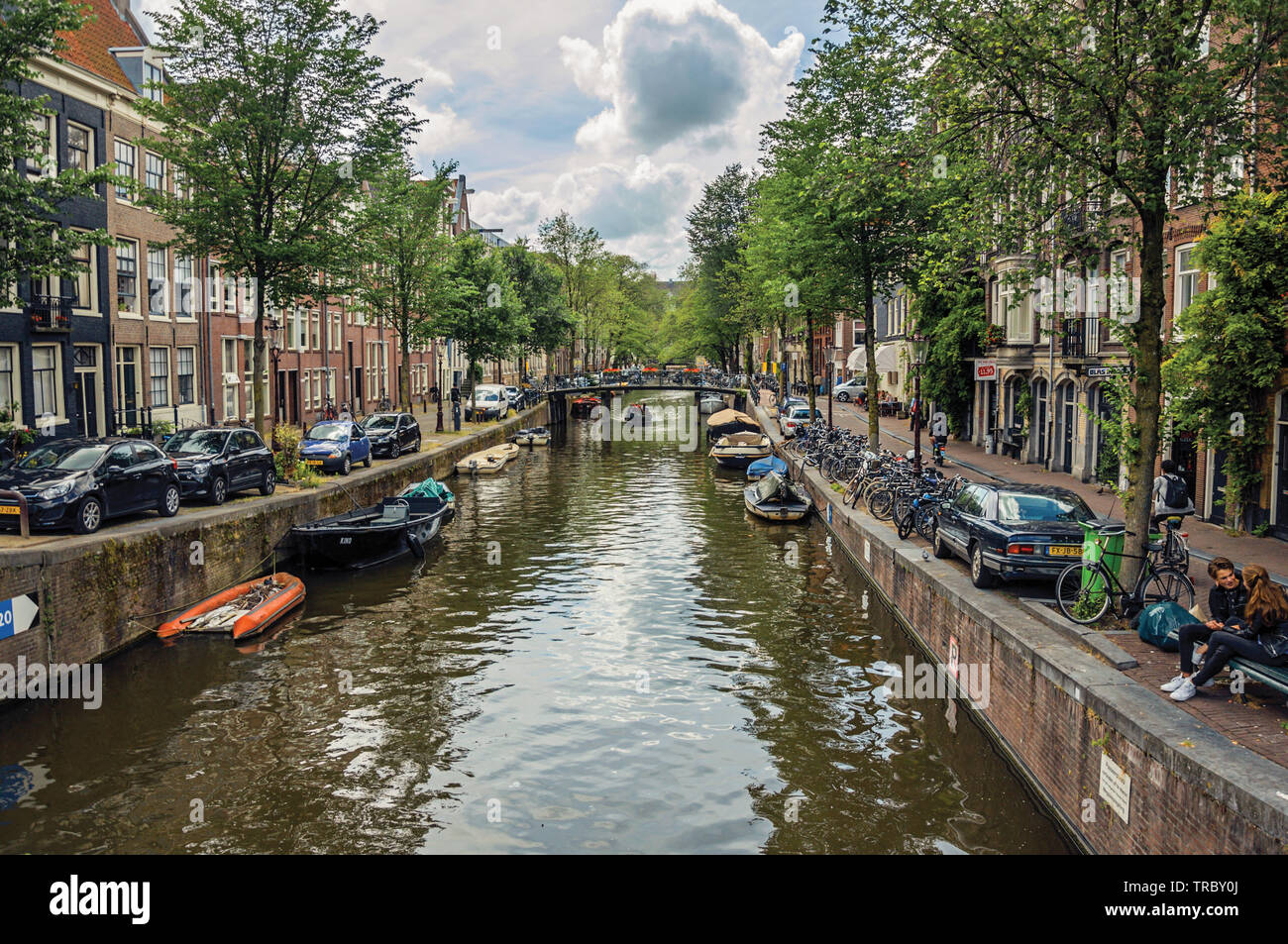 Canal with old brick buildings, boats and cloudy blue sky in Amsterdam ...