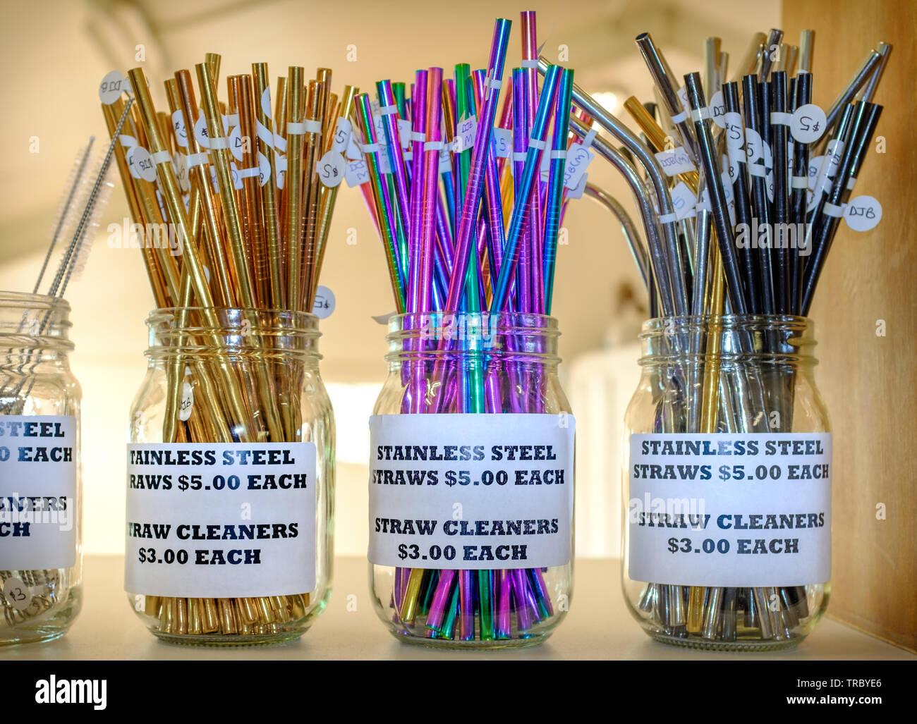 A shelf of colourful steel drinking straws in jars on display in shop ...