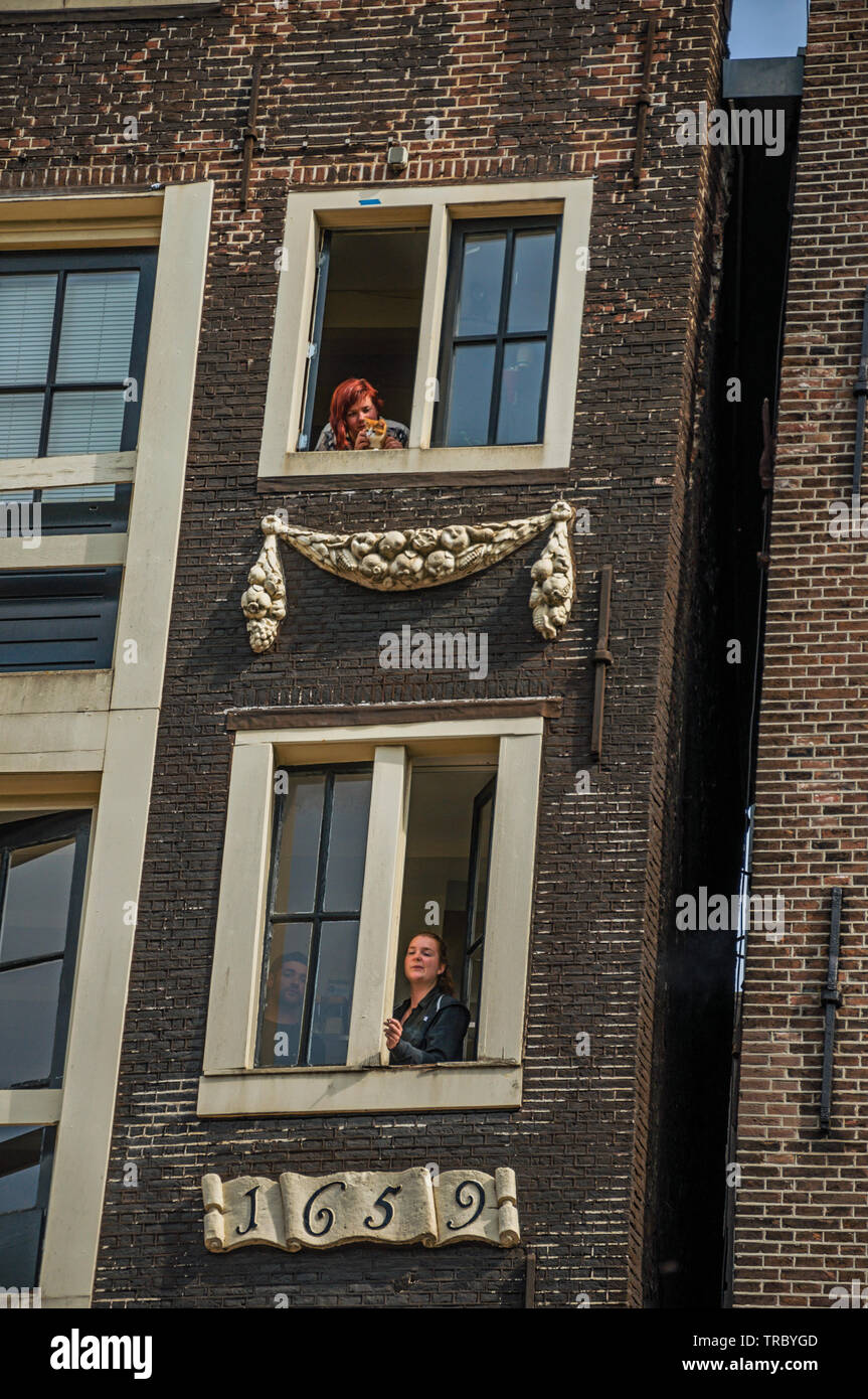 People on windows of old brick building with sunny blue sky in ...