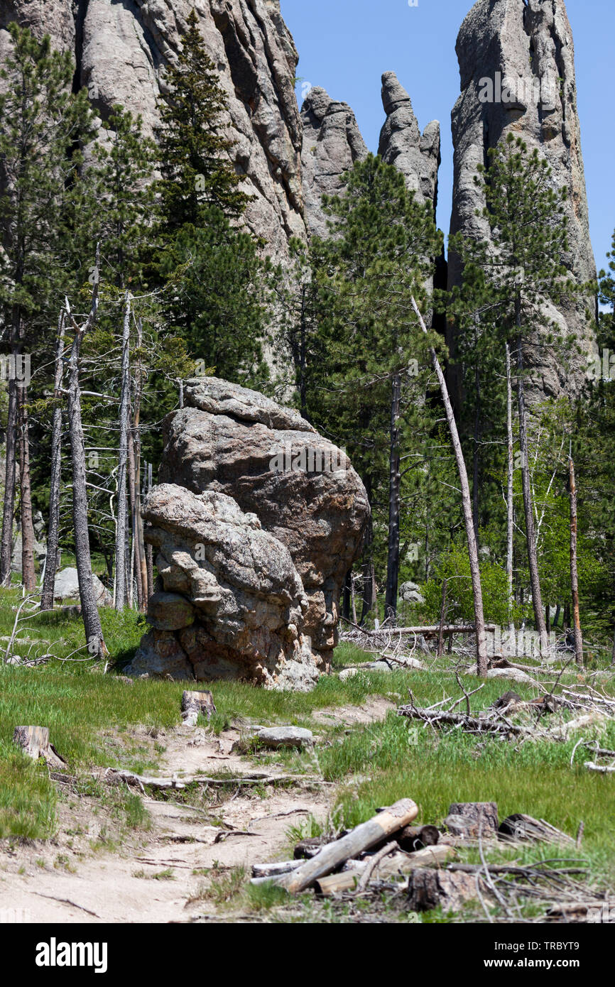 A hiking trail leading past a large boulder with tall cathedral spires ...