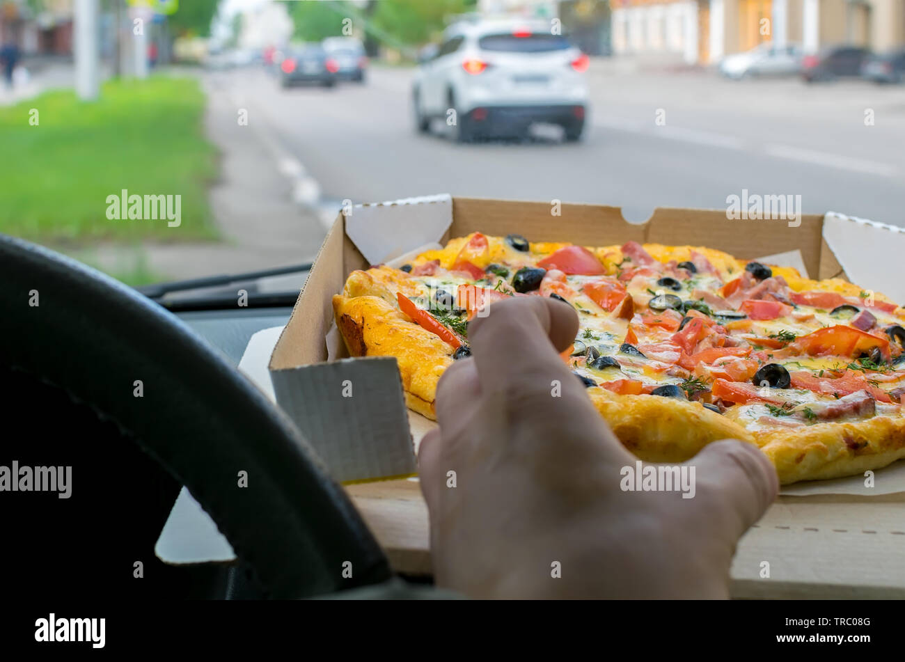 the driver hand takes a piece of pizza, the packaging of which lies on ...
