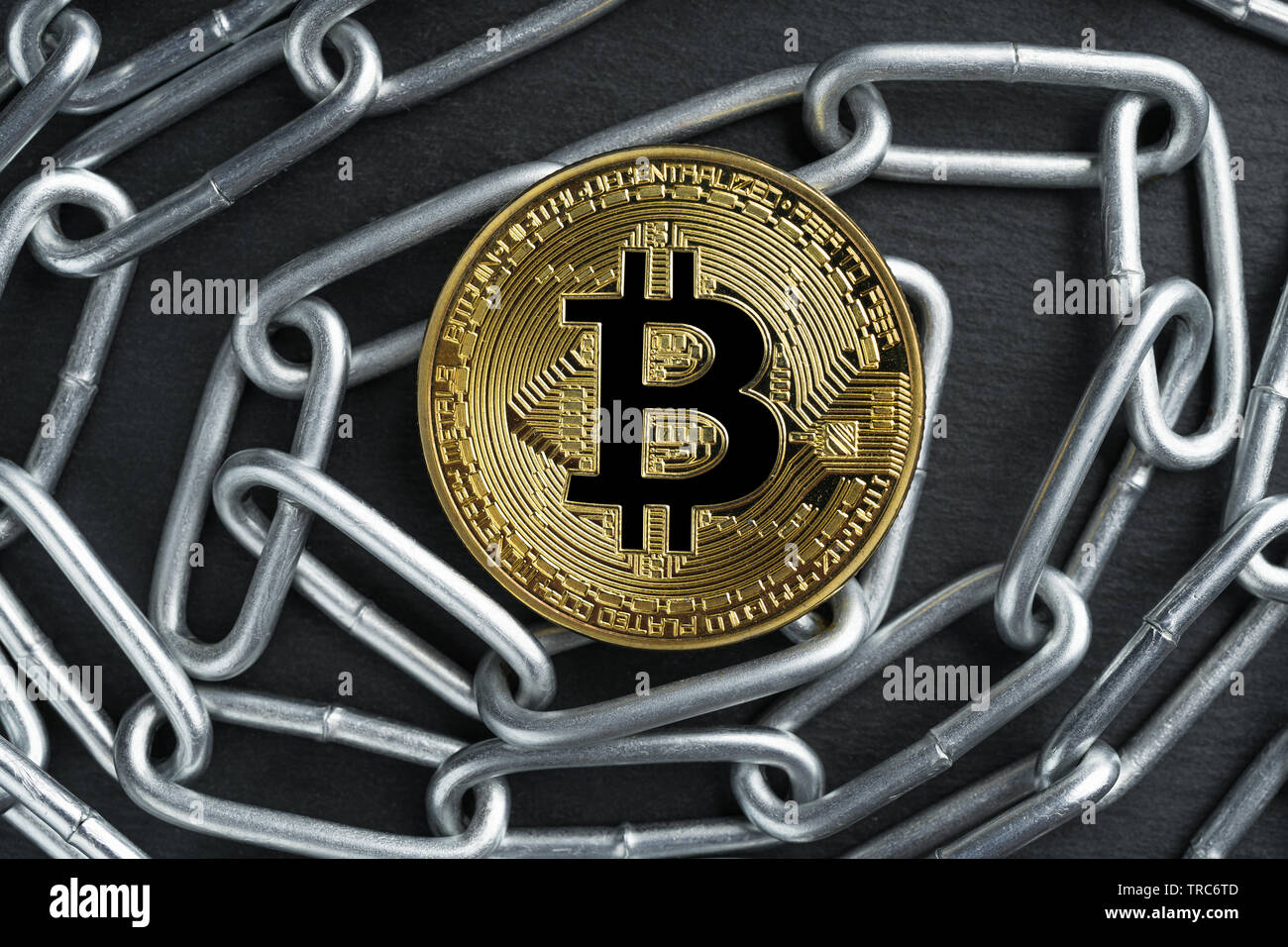 Physical Bitcoin gold coin on a convoluted shiny metal chain on dark ...