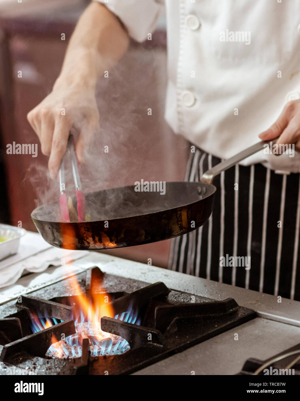 Chef cooking with flame in a frying pan on a kitchen stove Stock Photo ...