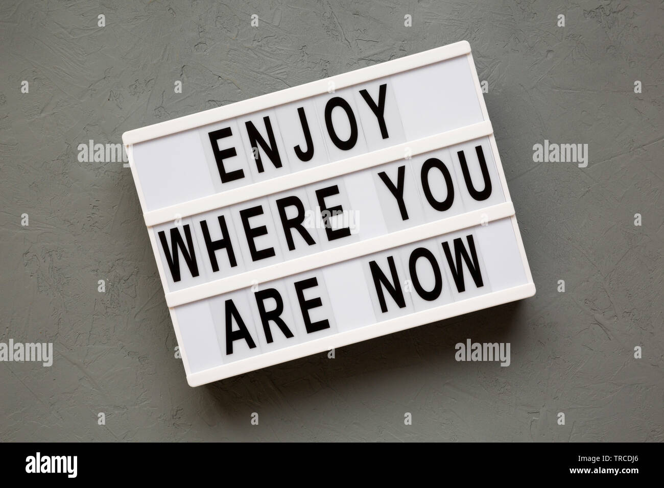'Enjoy where you are now' words on modern board over concrete surface ...