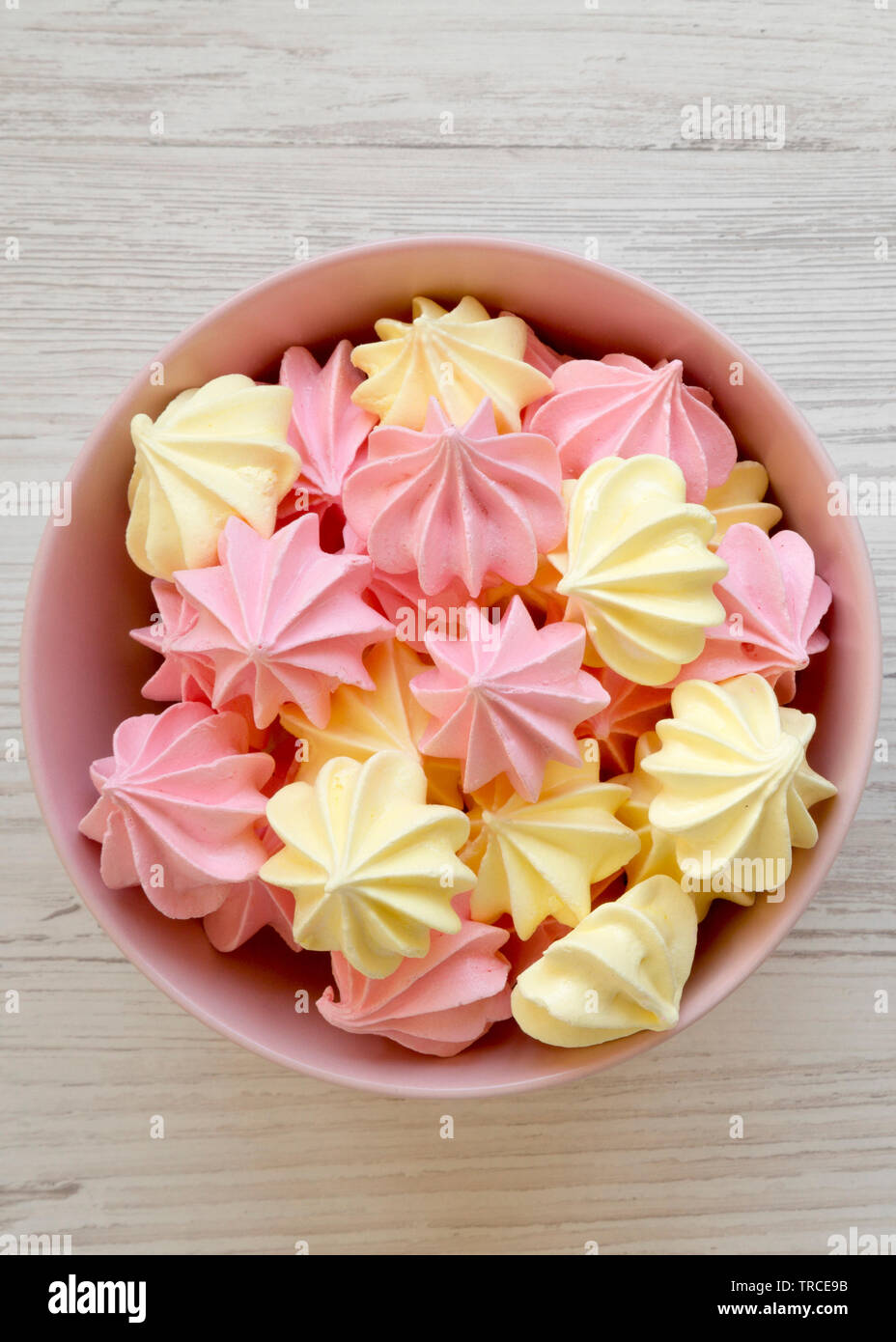 Mini meringues in a pink bowl over white wooden background, overhead ...