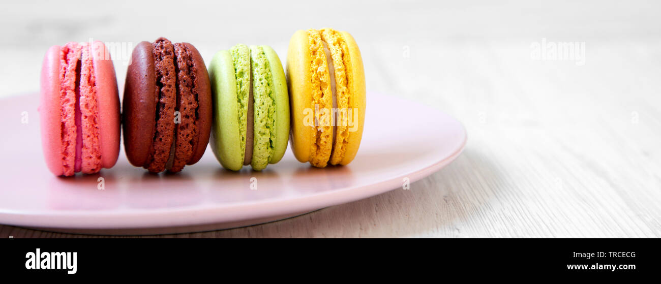 Sweet and colorful macarons on pink plate over white wooden background ...