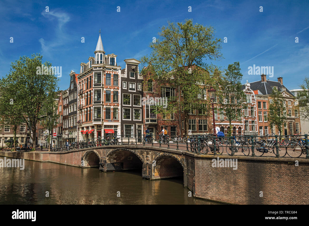 Bridge on canal with brick buildings, people and cyclists in Amsterdam ...
