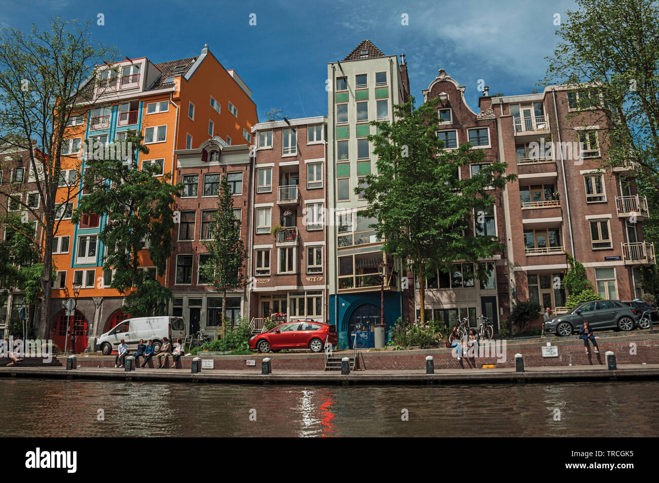 Tree-lined canal with old brick buildings, people and blue sky in ...