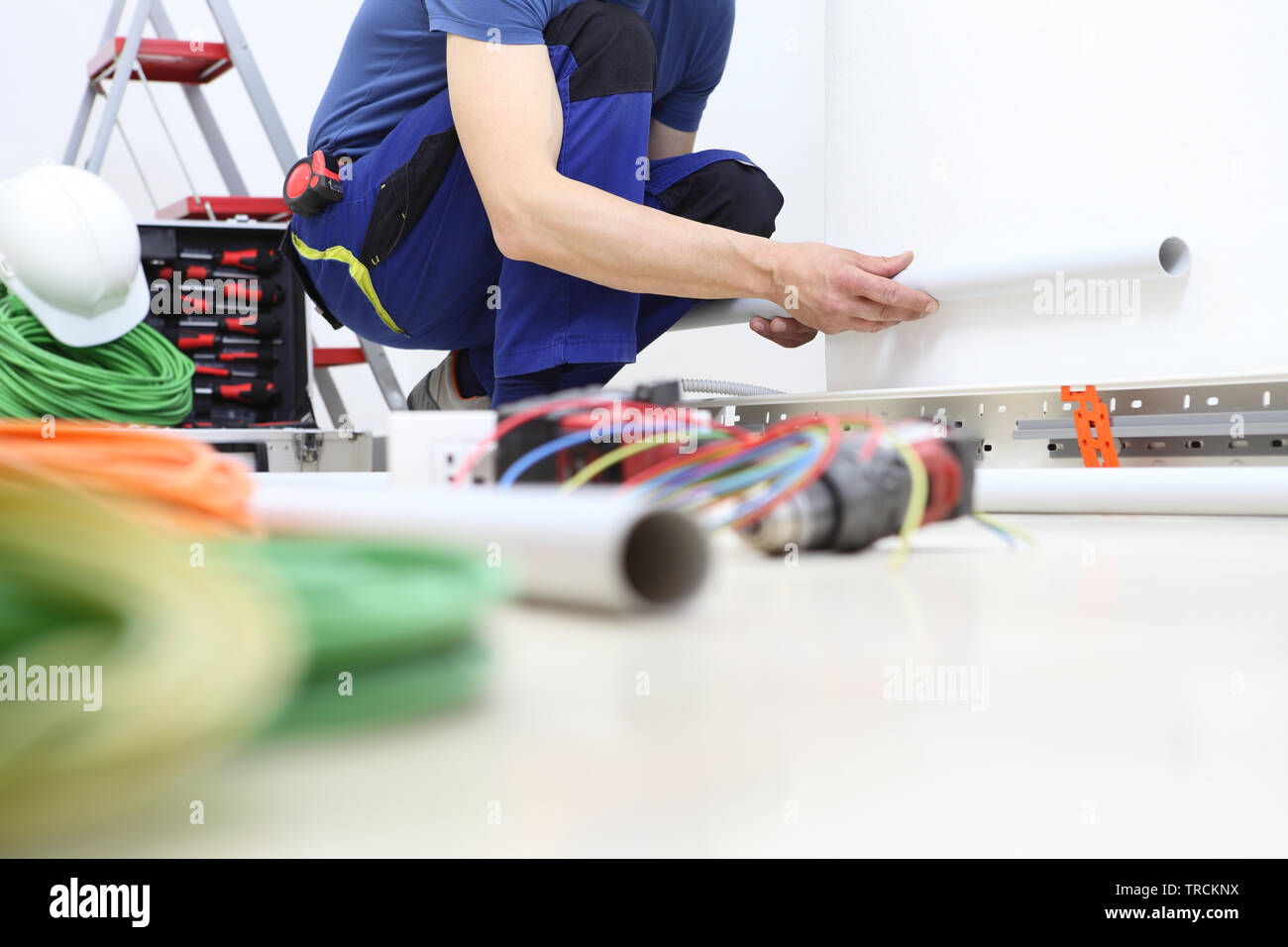 electrician at work with the plastic pipe in his hand to pass the ...