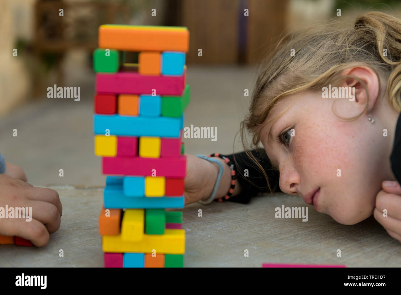 A child removes an orange wooden block from a tower with stacked wooden ...