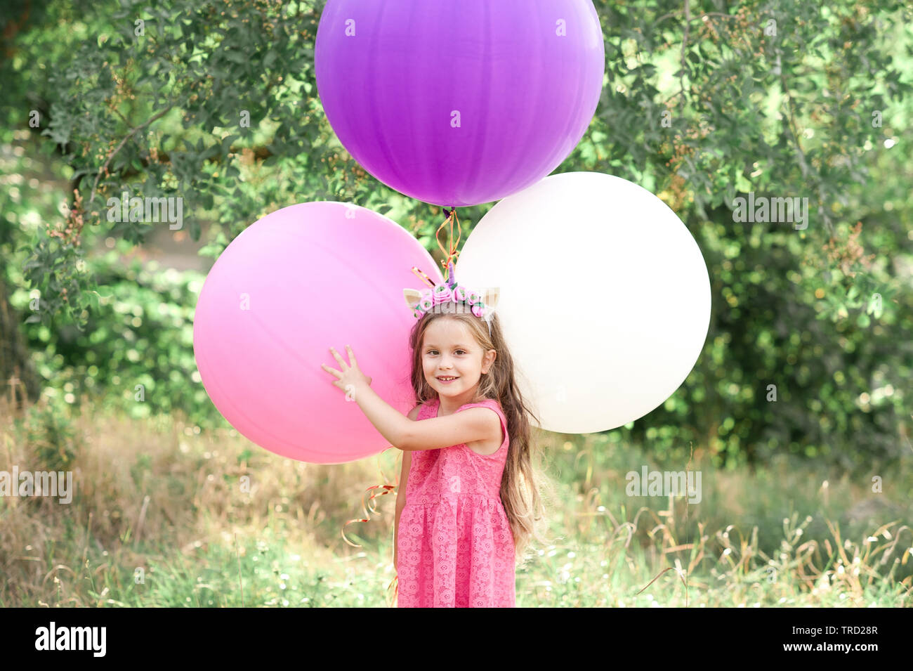 Smiling baby girl 5-6 year old holding big balloons over nature ...