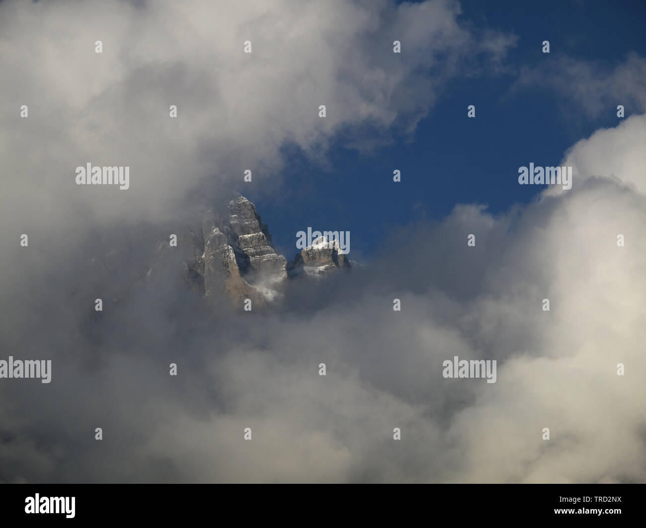 blue sky and the mighty cliff face of a steep mountain emerge behind a ...