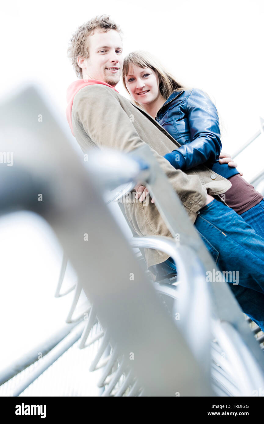 Portrait of a young couple hugging and smiling into the camera outdoors ...