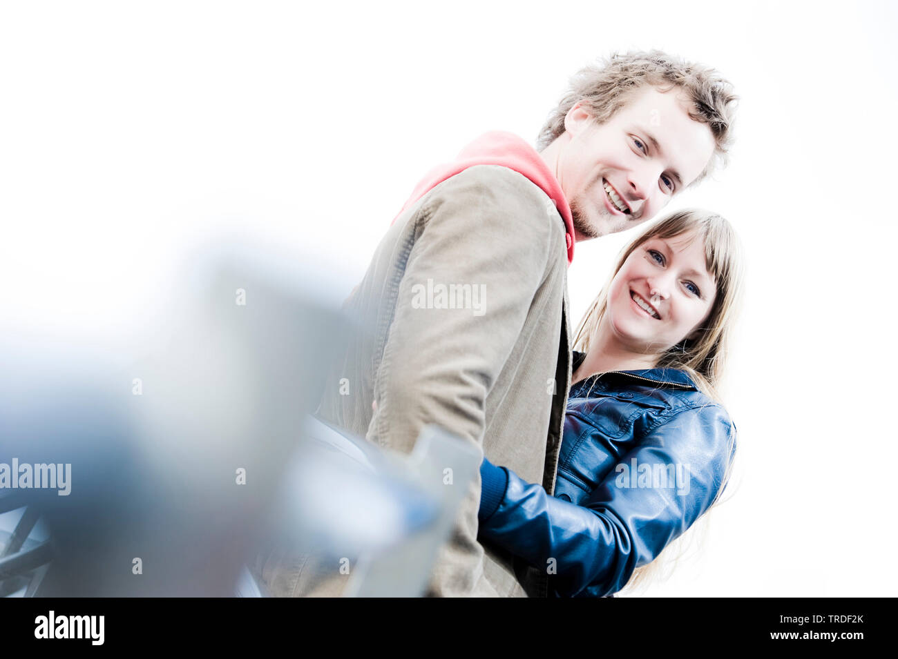Portrait of a young couple hugging and smiling into the camera outdoors ...