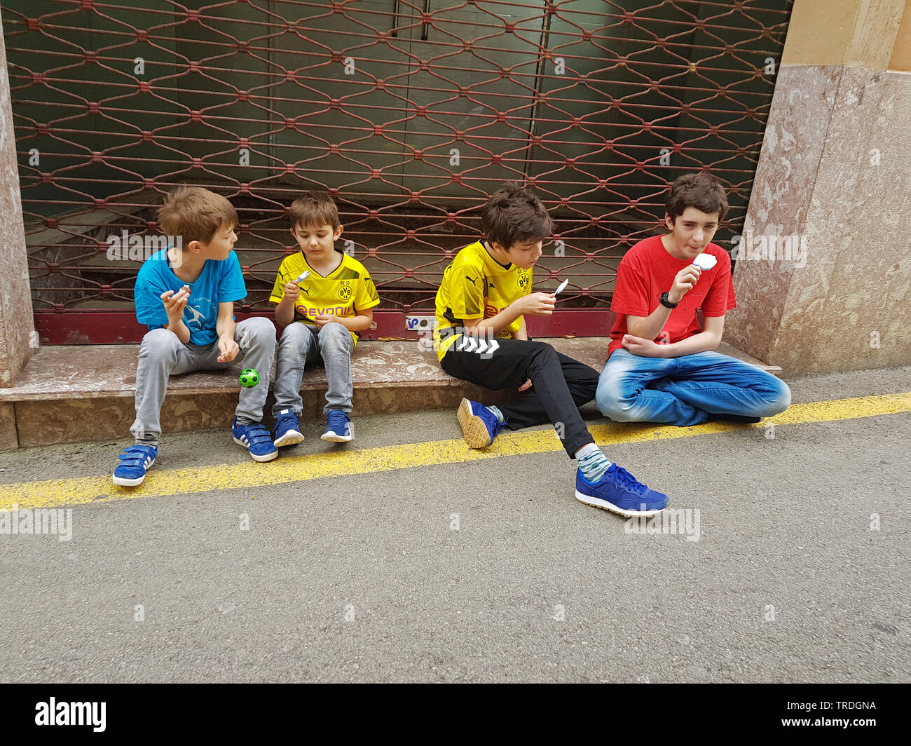 four children sitting on a pavement eating eis, Spain, Balearic Islands ...
