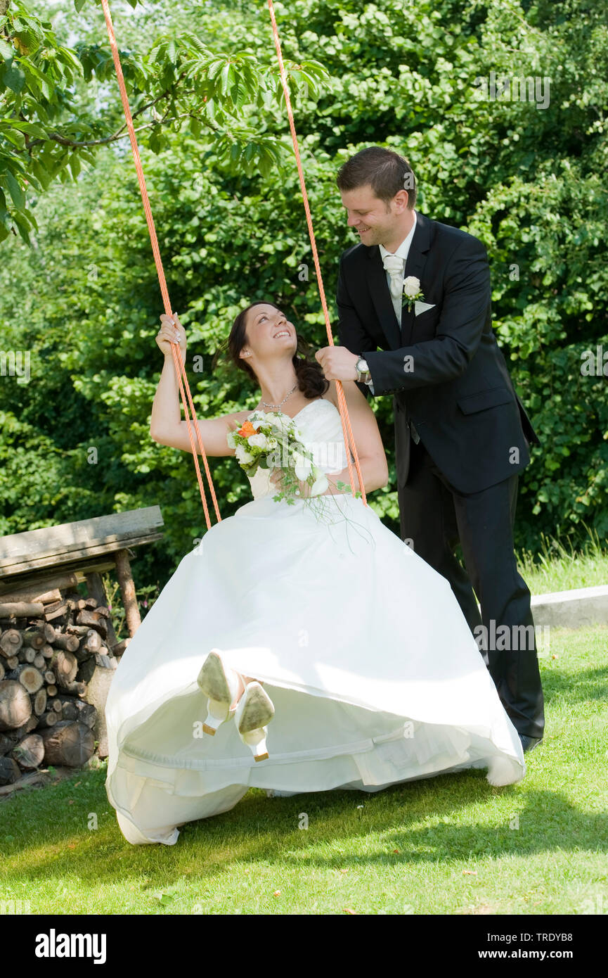 Wedding picture of a bride on a swing with the groom standing aside ...