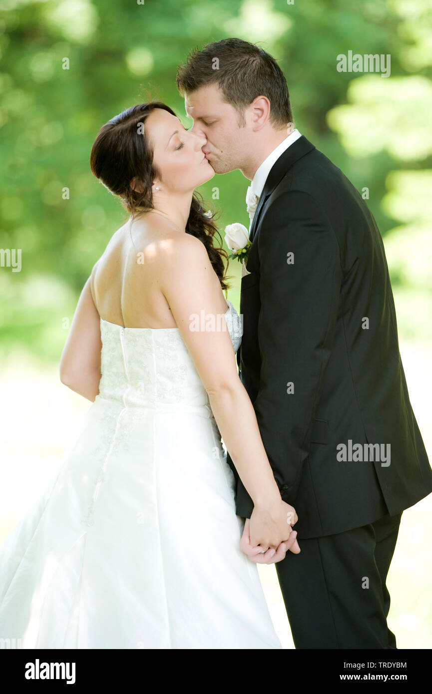 Wedding picture of a bridal couple holding hands and kissing outdoors ...