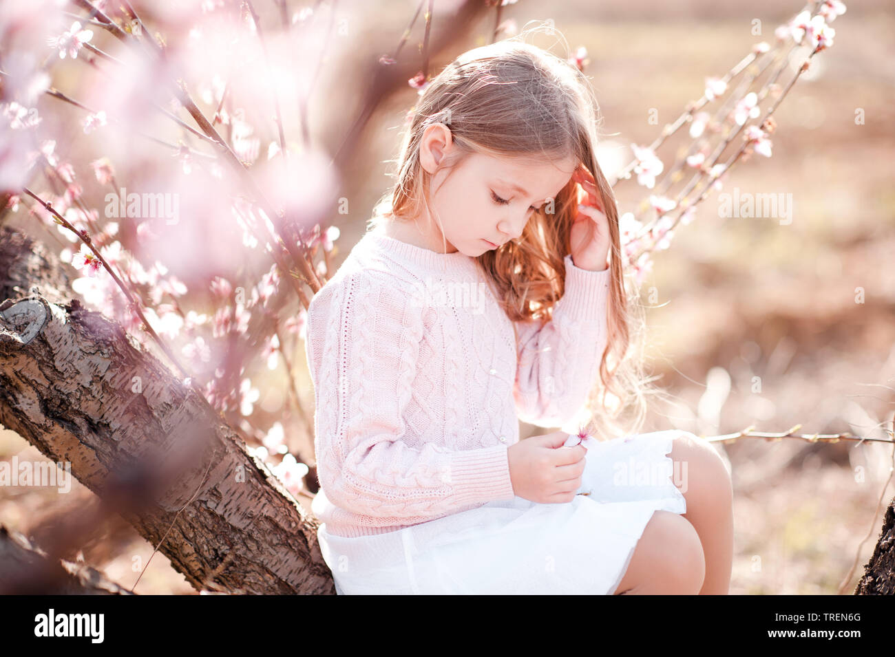 Cute baby girl sitting on tree playing with flowers outdoors. Childhood ...