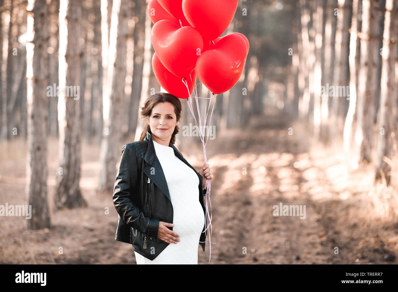 Smiling pregnant woman holding heart shape balloons outdoors. Looking ...