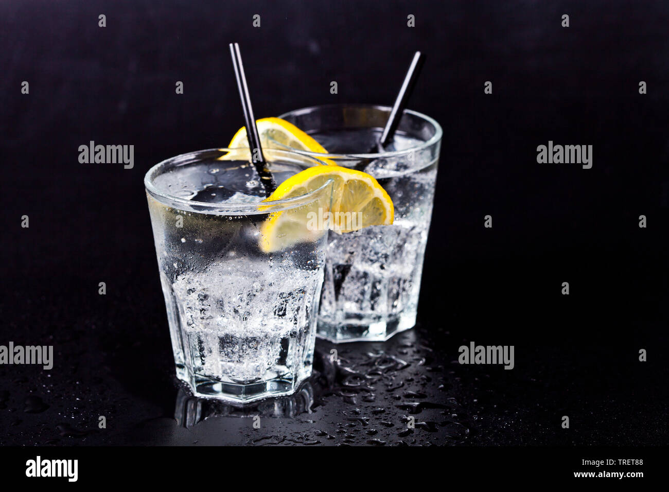 Two glasses of fresh cold carbonated water with ice cubes and lemon slices. Soda water on black ...