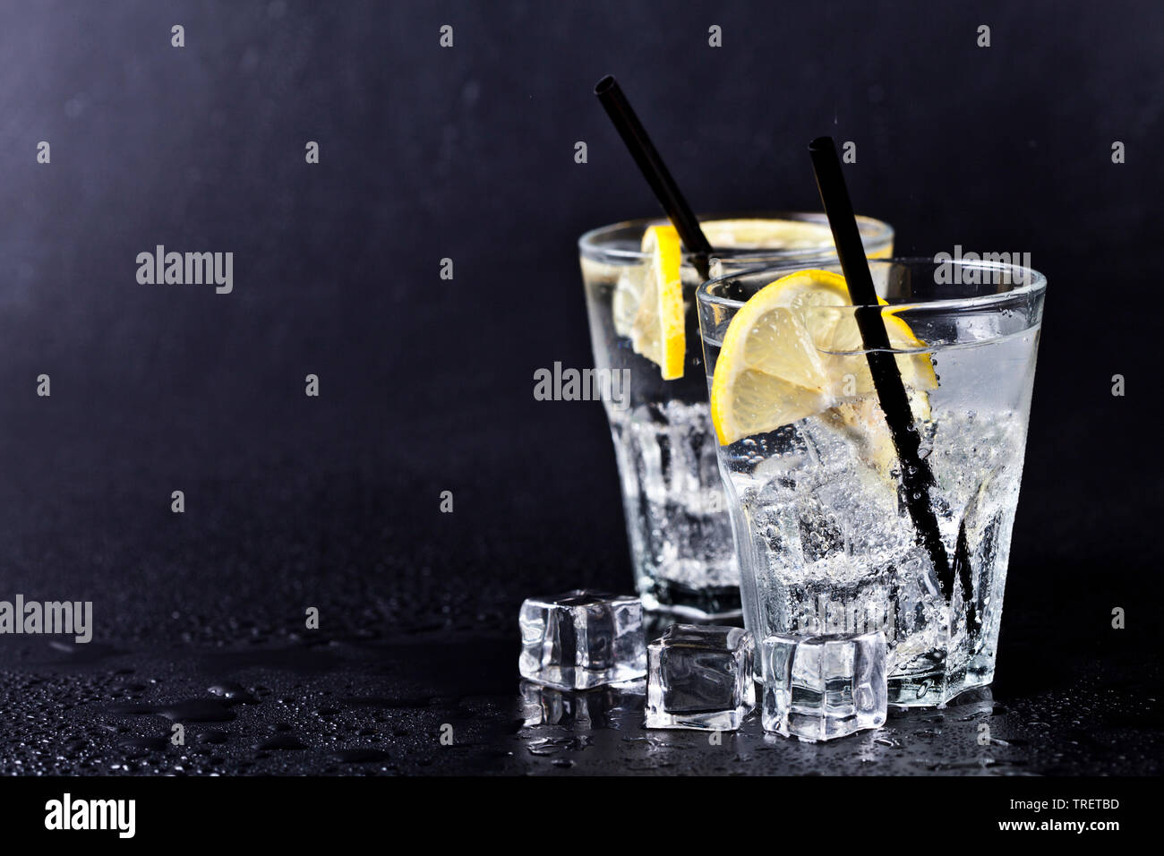 Glasses of fresh cold carbonated water with ice cubes and lemon slices. Soda water on black ...