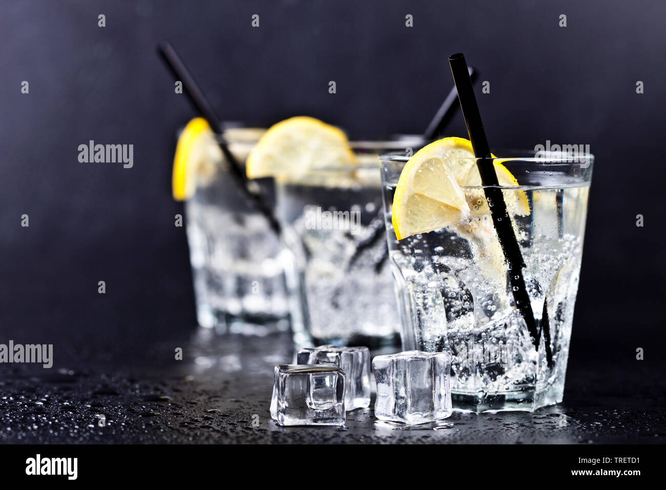 Three glasses with fresh cold carbonated water with lemon slices and ice cubes closeup. Soda ...