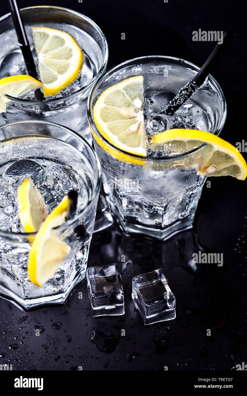 Three glasses with fresh cold carbonated water with lemon slices and ice cubes closeup. Soda ...