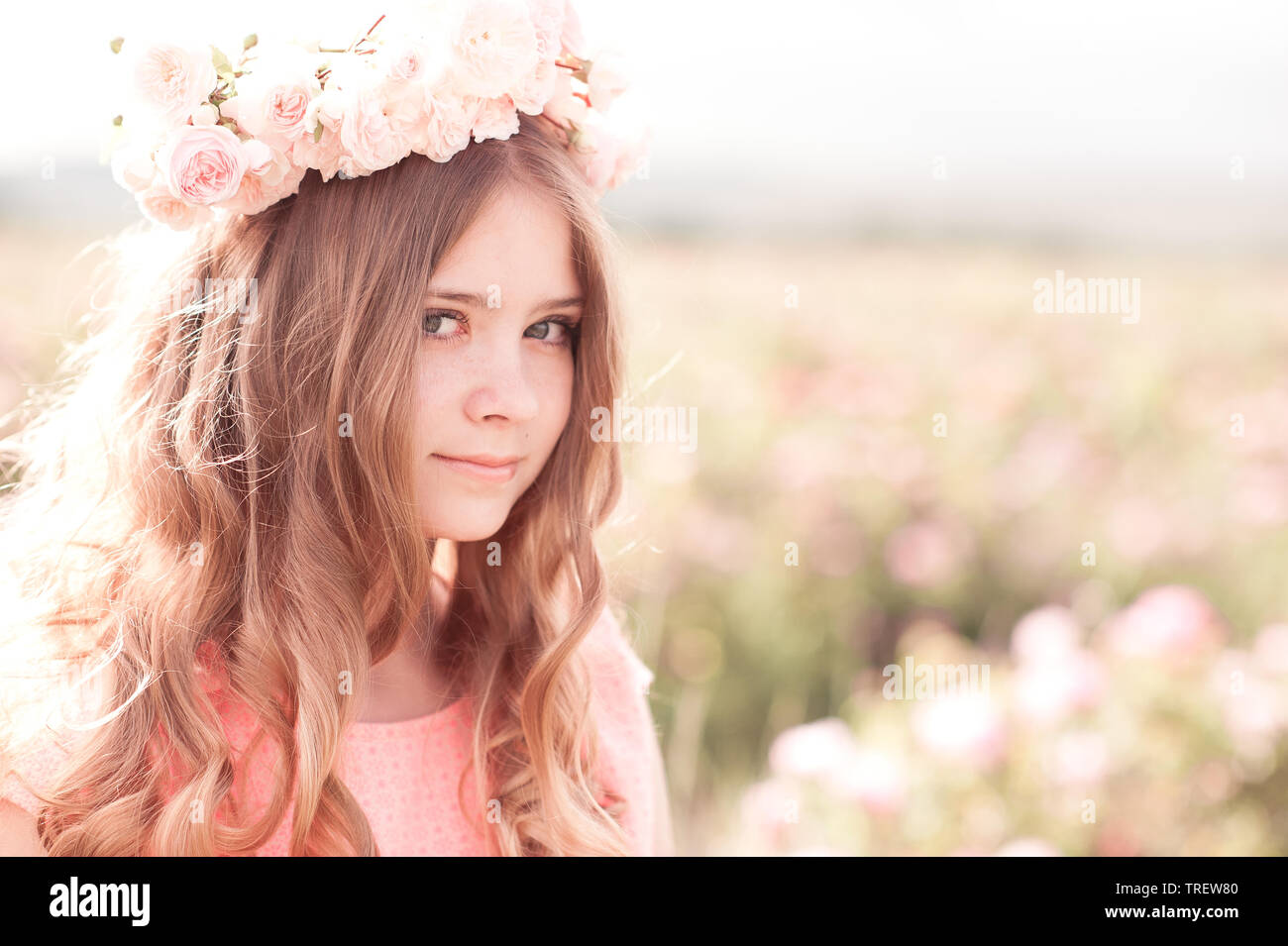 Smiling blonde girl 14-16 year old posing with roses wreath outdoors ...