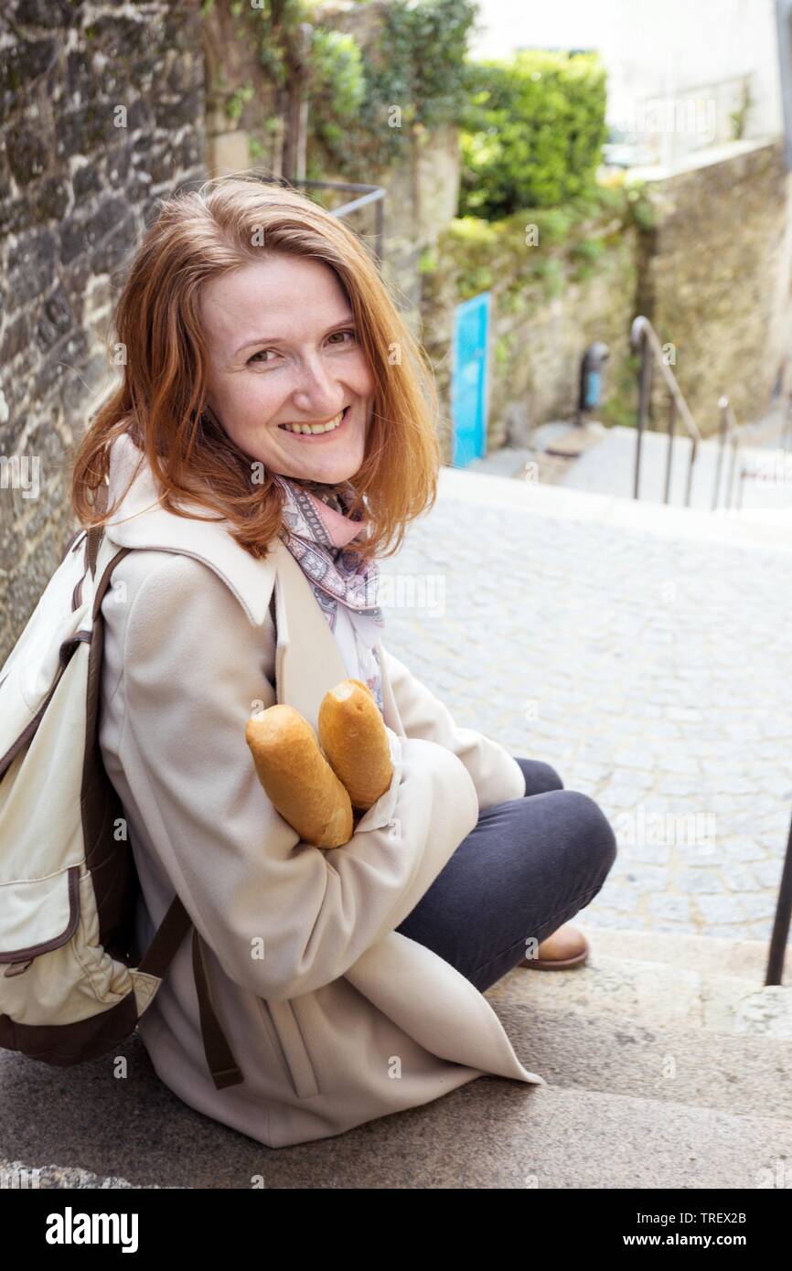 smiling French girl with baguettes on the street side of the city ...