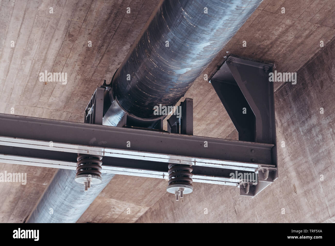 Pipe under a concrete bridge with dampers and steel support to keep it ...
