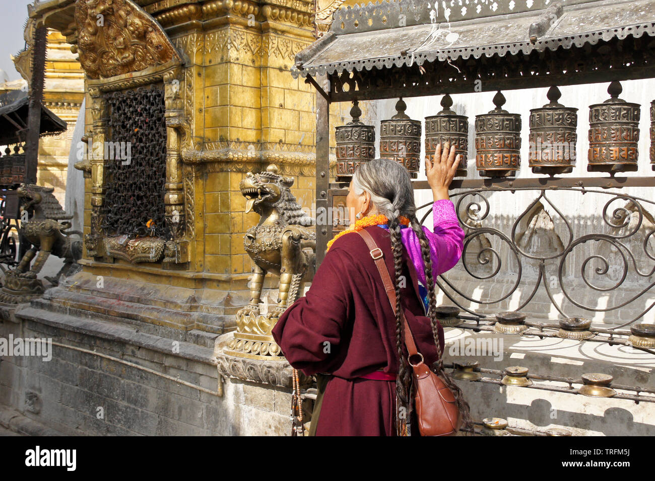 Tibetan woman in traditional dress spinning prayer wheels at a gilded ...