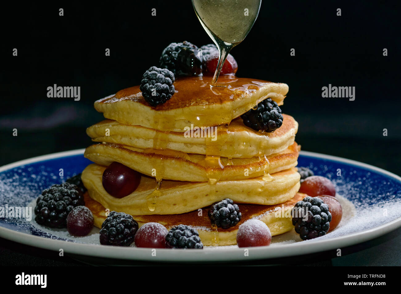 Dripping syrup onto a stack of pancakes with summer fruits. Isolated on ...