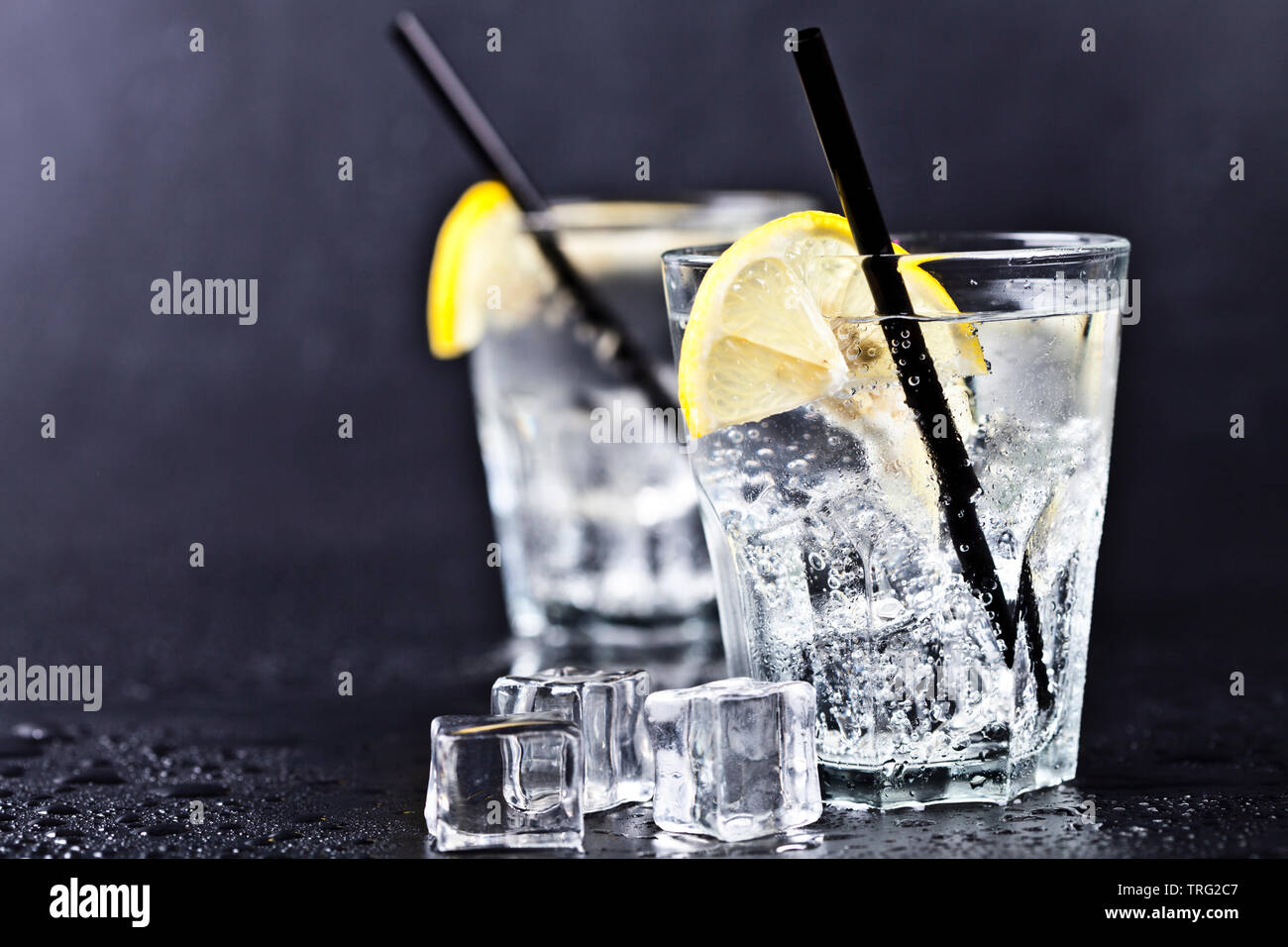 Glasses of fresh cold carbonated water with ice cubes and lemon slices. Soda water on black ...