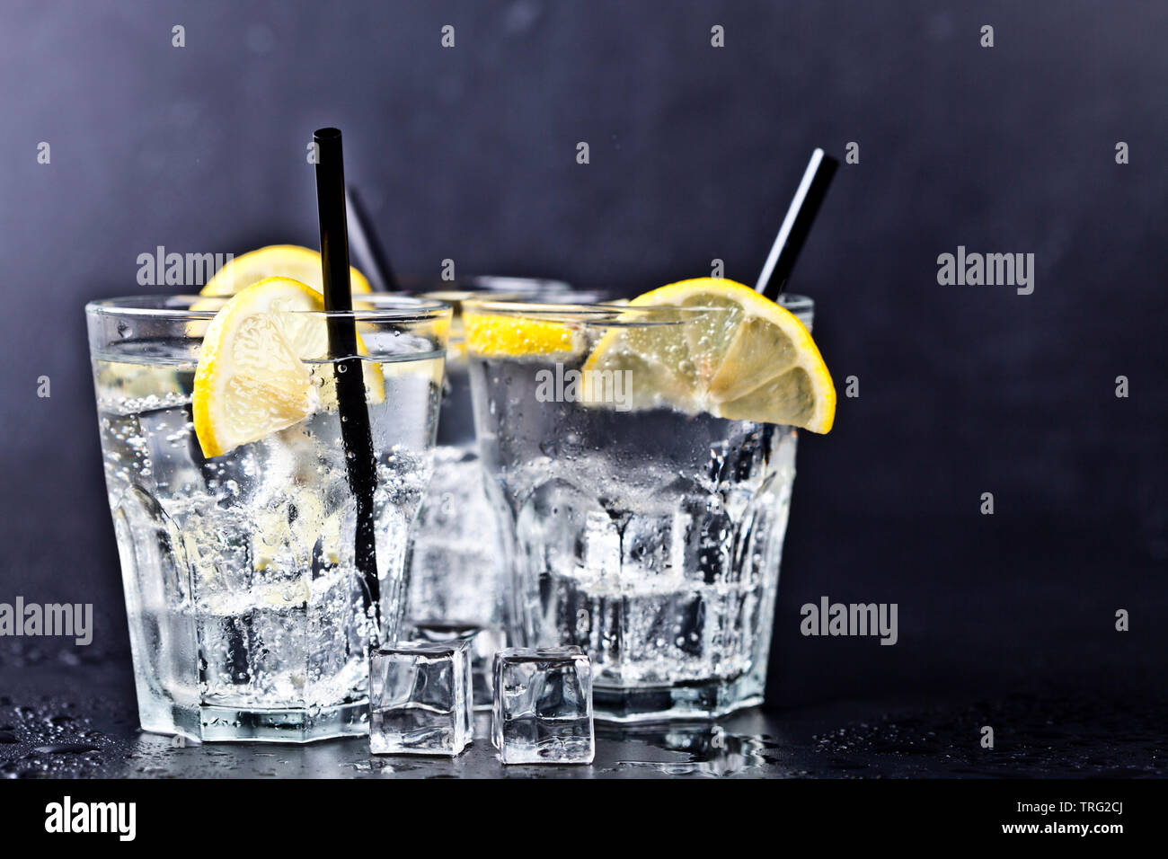 Three glasses with fresh cold carbonated water with lemon slices and ice cubes closeup. Soda ...