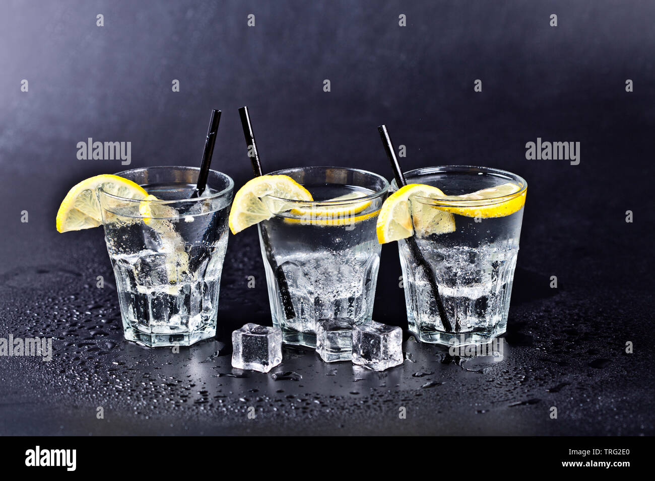 Three glasses of fresh cold carbonated water with ice cubes and lemon slices. Soda water on ...