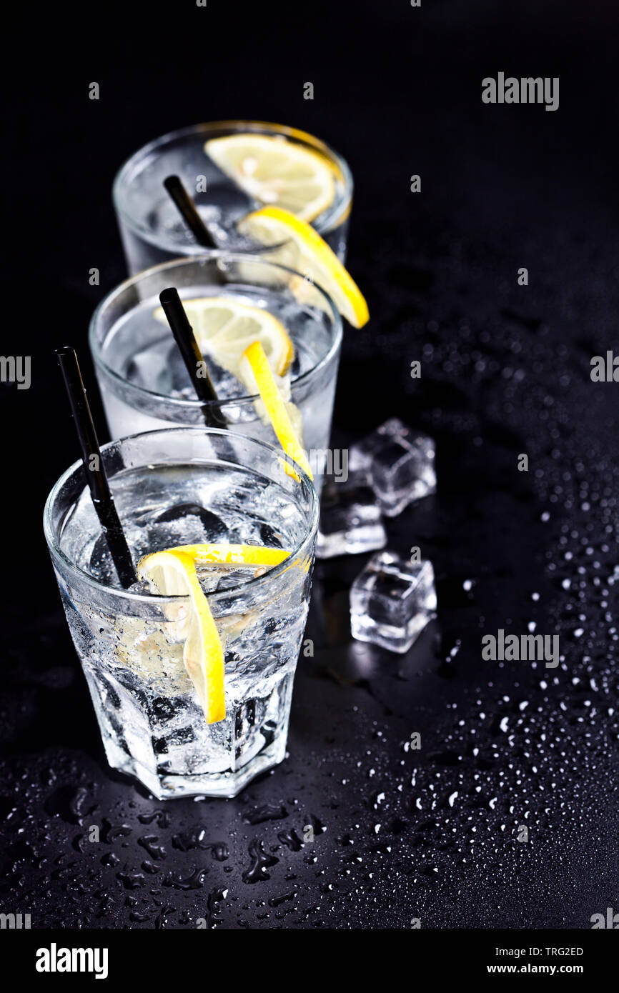 Three glasses with fresh cold carbonated water with lemon slices and ice cubes closeup. Soda ...