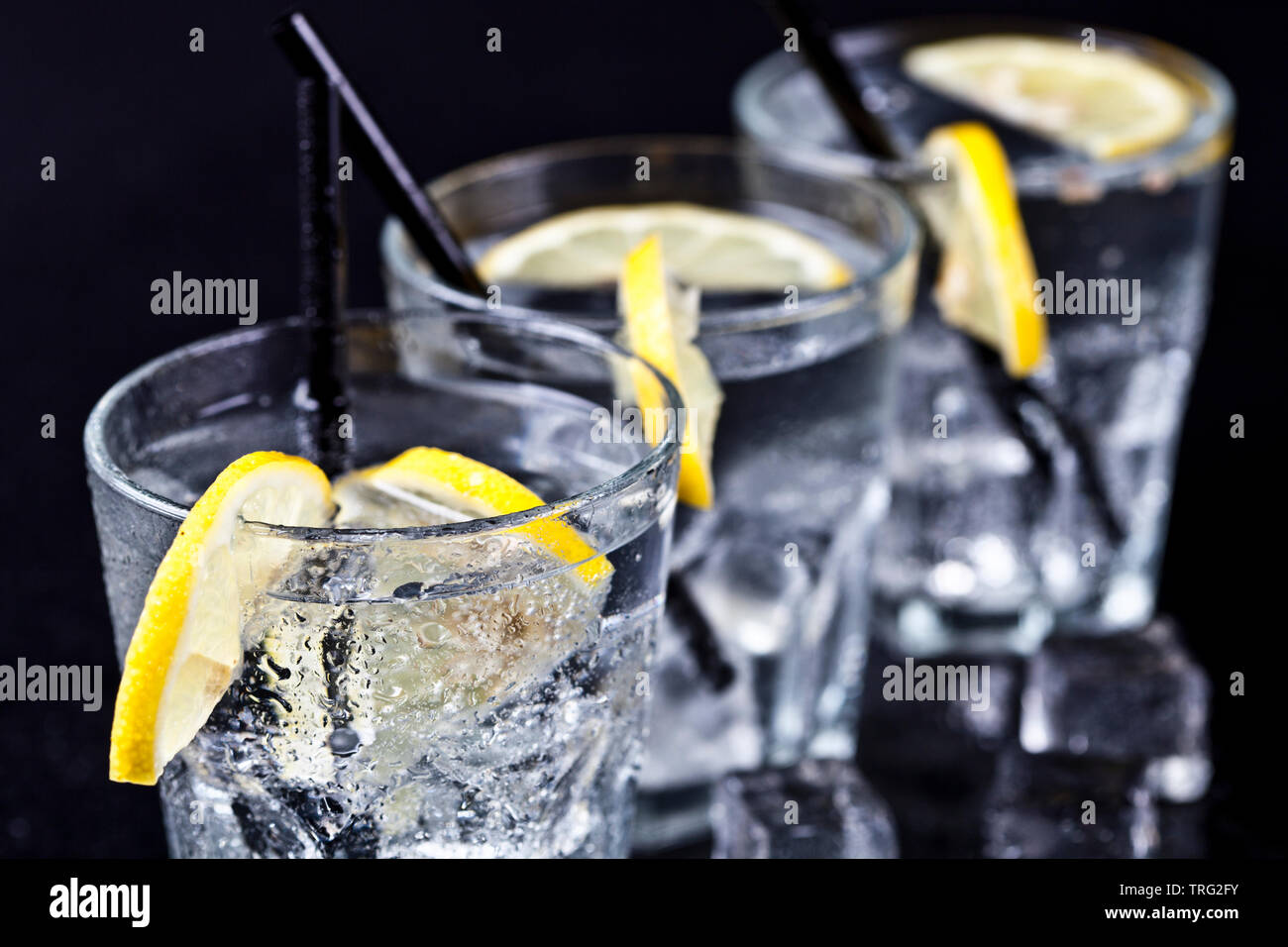 Three glasses with fresh cold carbonated water with lemon slices and ice cubes closeup. Soda ...