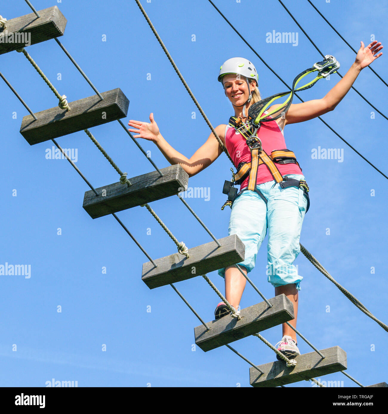 Young woman passing a rope bridge in high ropes course at a sunny day ...