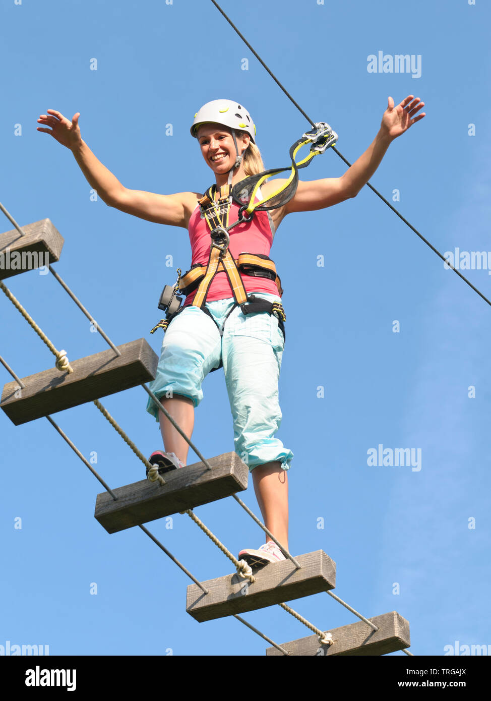 Young woman passing a rope bridge in high ropes course at a sunny day ...