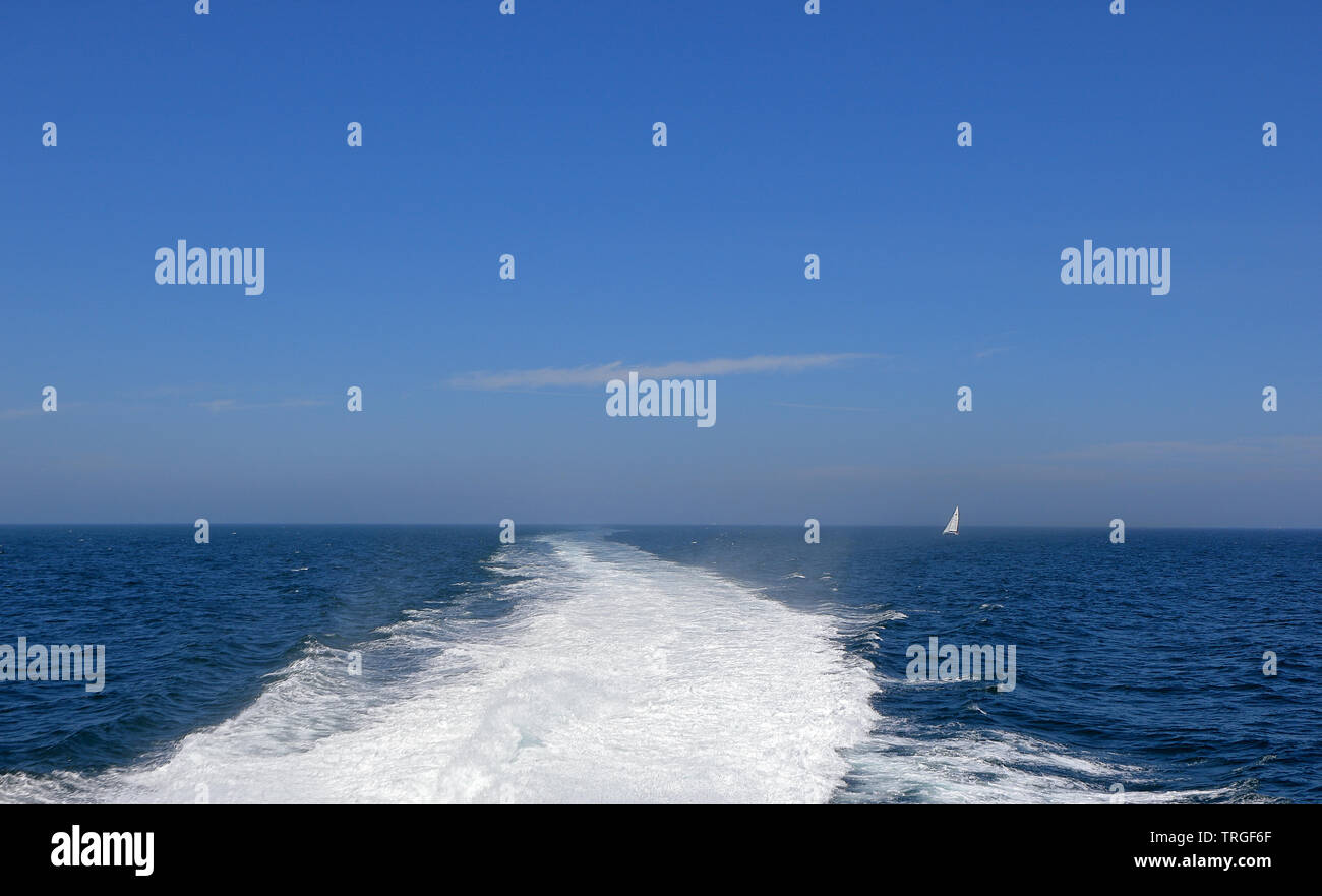Boat wake in the sea on a brilliant sunny day with distant sailboat ...