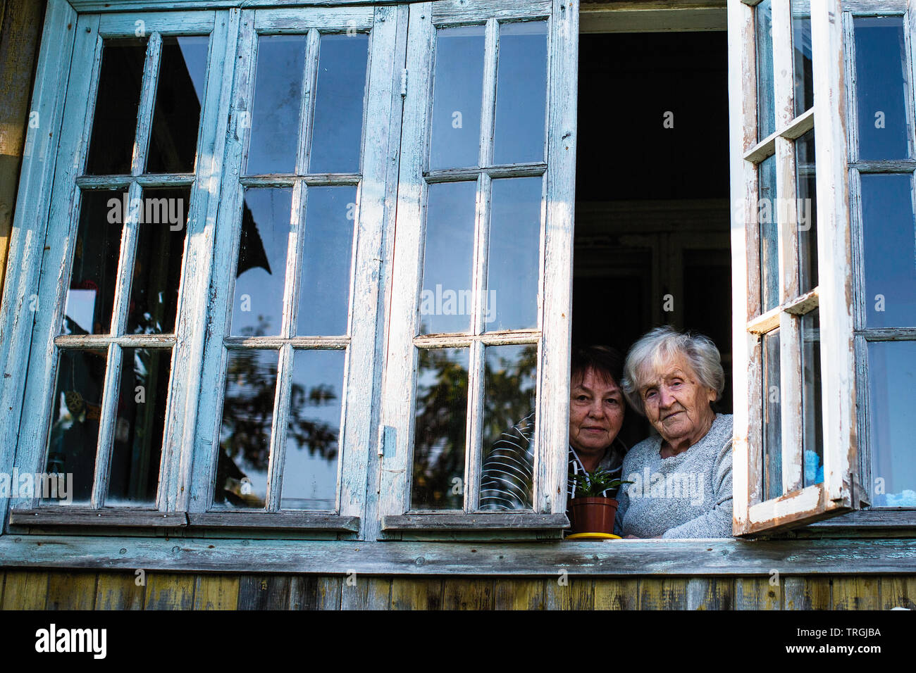 Old grandmother and her adult daughter on the window of village house ...