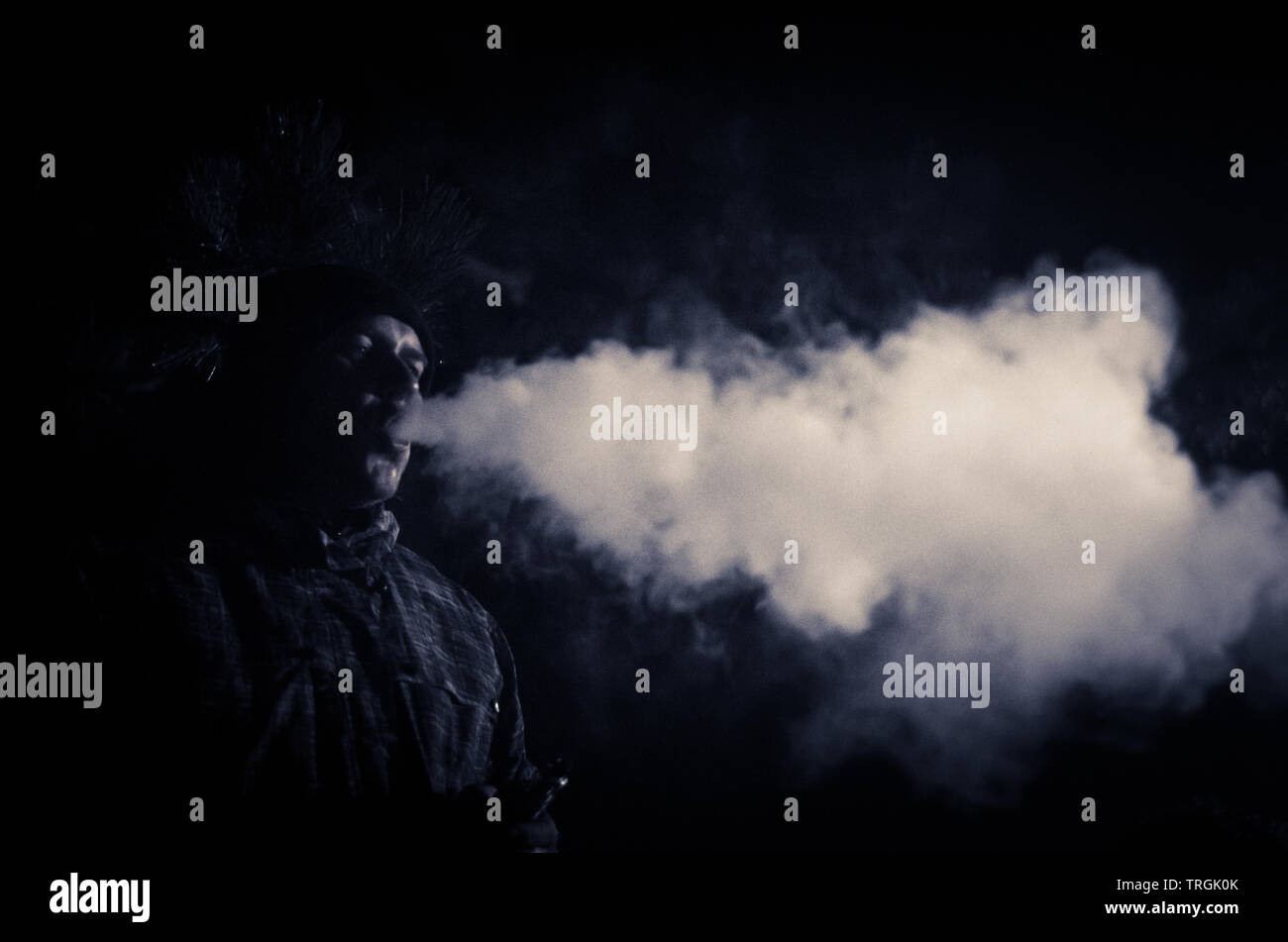 adult man smoking at night making a big smoke effect in back light ...