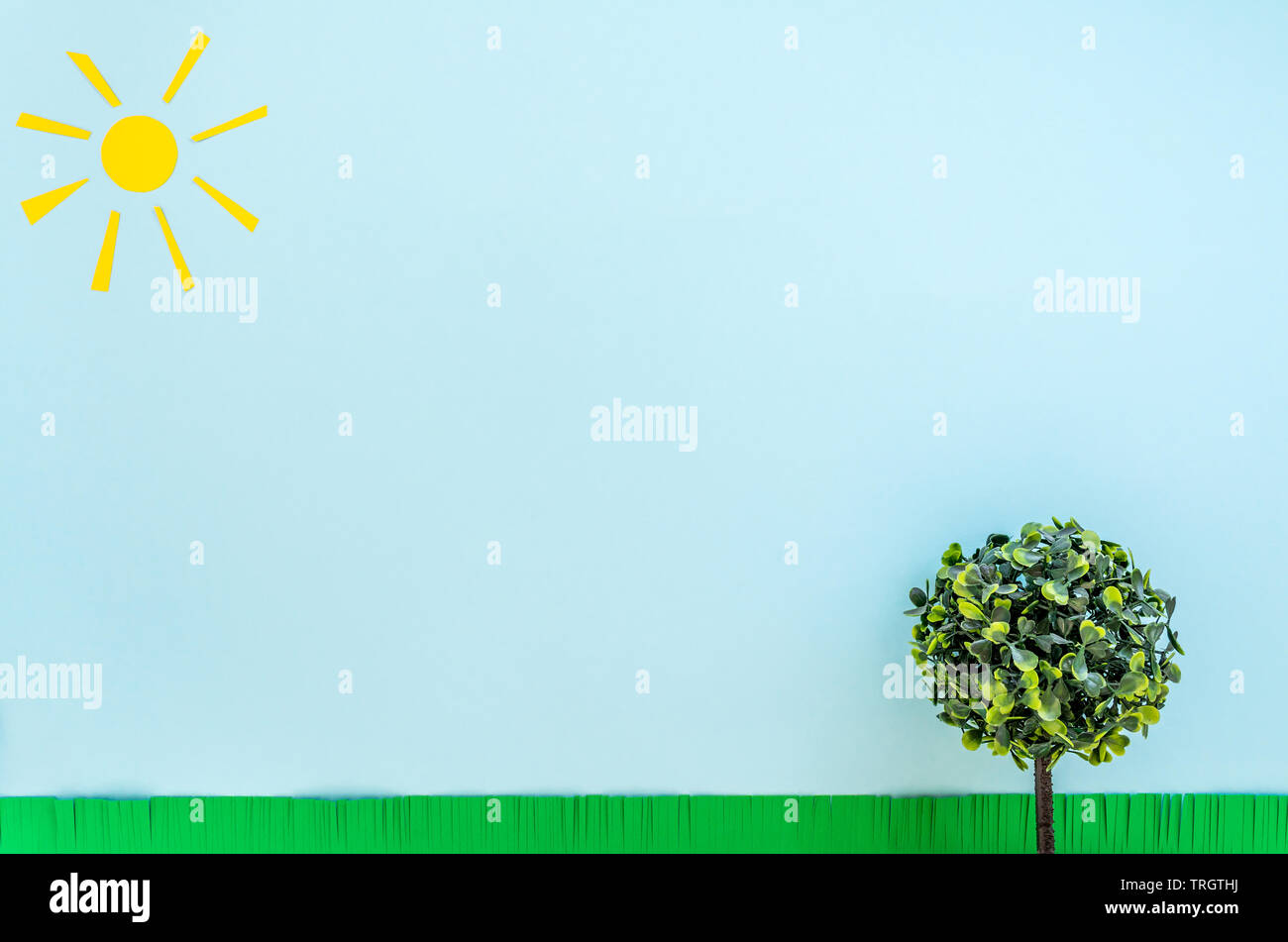 Paper sun, green grass and toy tree with green leaves on a blue ...