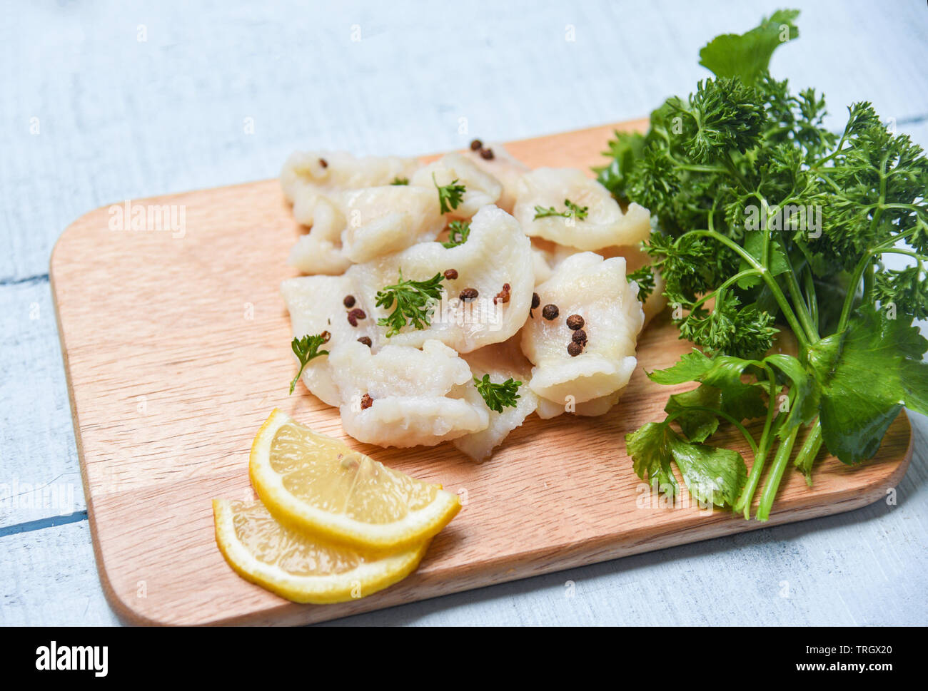 Cooked fish fillet piece with lemon and spices on wooden cutting board ...